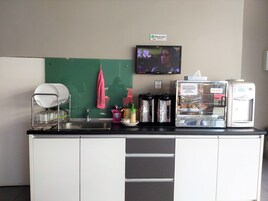 Uma cozinha compacta com pia, escorredor de louça, máquina de café e geladeira.