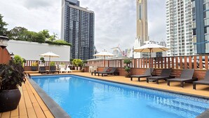 Piscina no terraço com espreguiçadeiras e guarda-sóis, cercada por edifícios altos.