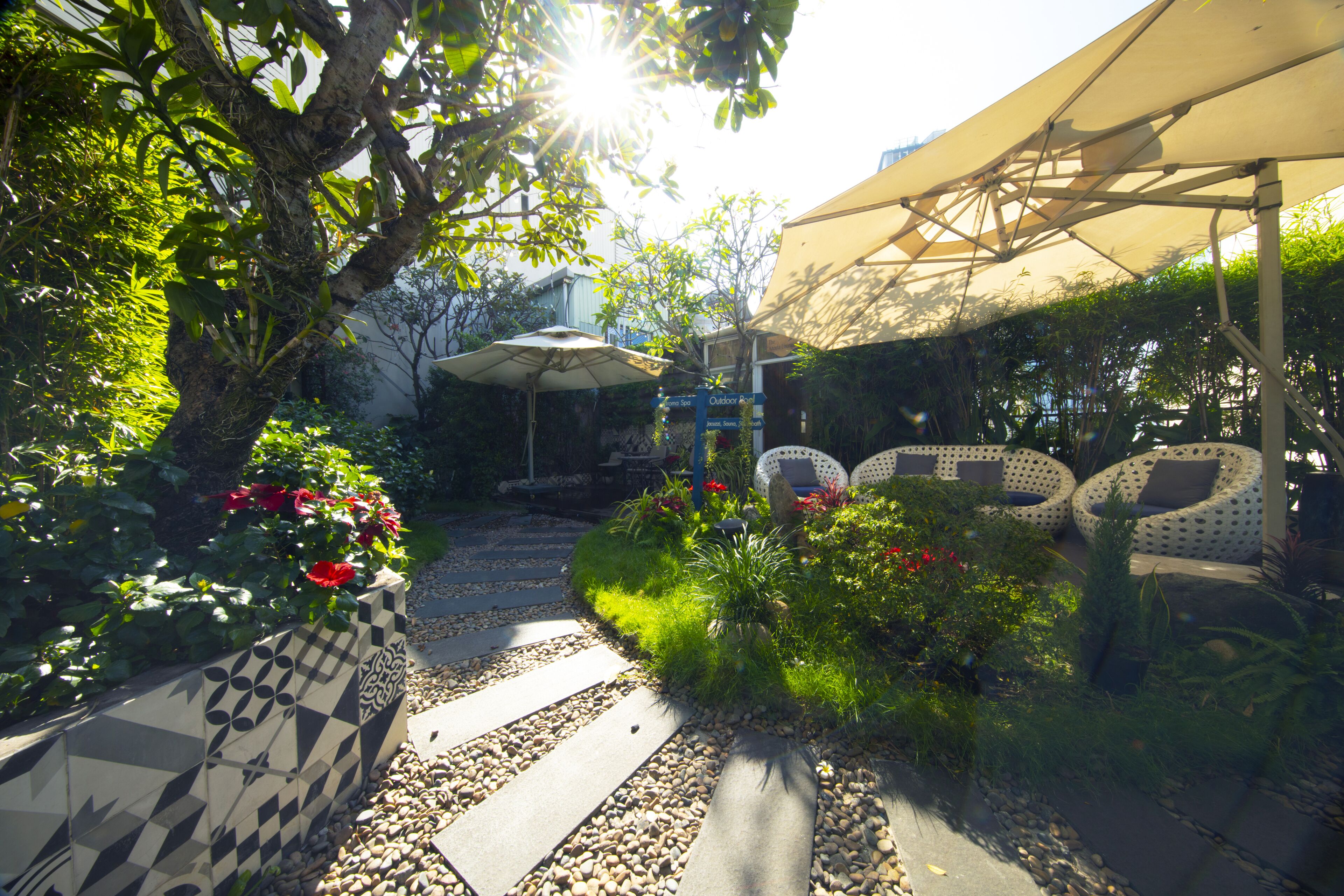 Um pátio com jardim, caminho decorado, área de estar externa e uma pérgula que oferece sombra.
