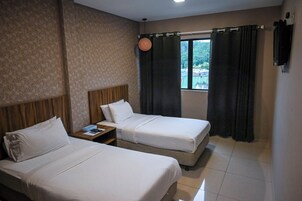 Quarto de hotel com duas camas, cabeceira de madeira, mesa de cabeceira, janela com cortinas e vista para o exterior.