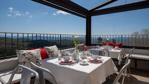Uma sala de jantar com mesas preparadas para um serviço de chá, com vista para uma paisagem montanhosa.