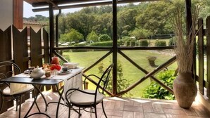 Uma área de refeições com mesa e cadeiras, vista para um jardim bem cuidado, e uma janela grande com moldura de madeira.