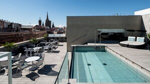 Uma área de piscina no terraço com assentos de lounge e vista para uma igreja histórica ao fundo.