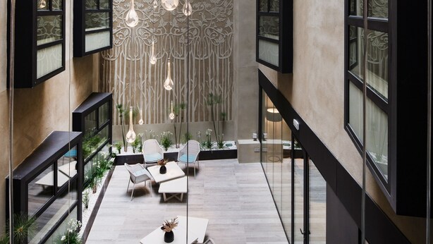 Um interior moderno com área de estar central, janelas amplas e luminárias pendentes.
