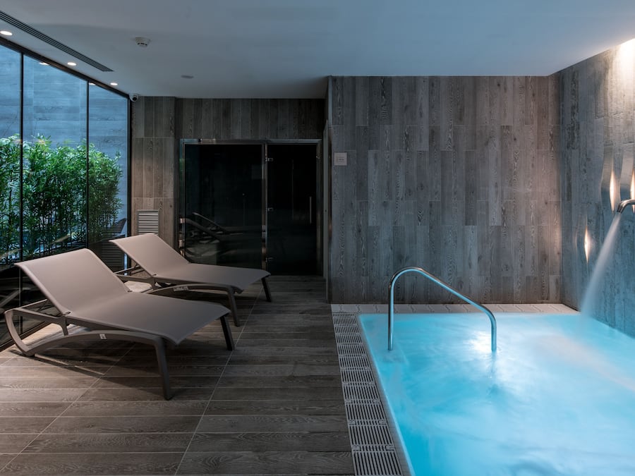 Uma área de spa moderna com hidromassagem, cadeiras de descanso e vista para o verde através de grandes janelas.