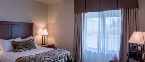 Quarto de hotel com cama, luminárias de cabeceira, janela com cortinas e uma cadeira.