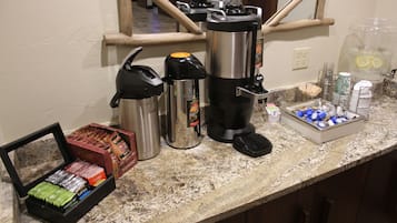 Uma bancada de cozinha com cafeteira, um termo, um bebedouro e uma caixa de saquinhos de chá.