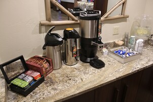 Uma bancada de cozinha com cafeteira, um termo, um bebedouro e uma caixa de saquinhos de chá.