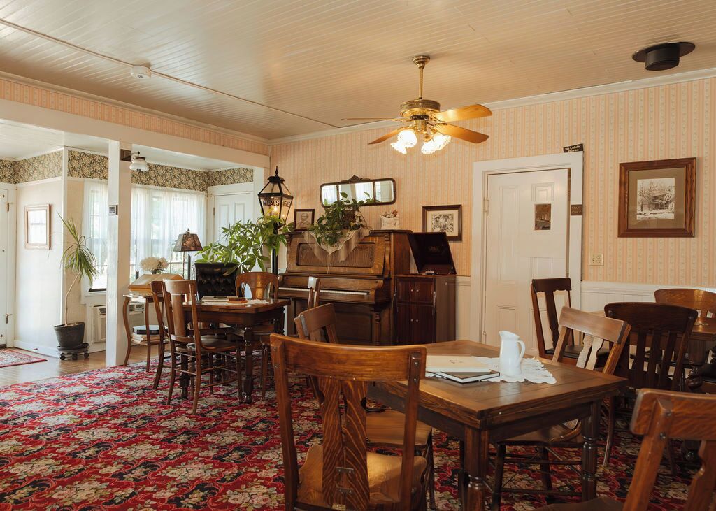 Uma sala de jantar com uma mesa de madeira, cadeiras, um piano e um ventilador de teto.