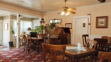 Uma sala de jantar com uma mesa de madeira, cadeiras, um piano e um ventilador de teto.
