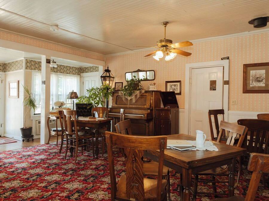 Uma sala de jantar com uma mesa de madeira, cadeiras, um piano e um ventilador de teto.
