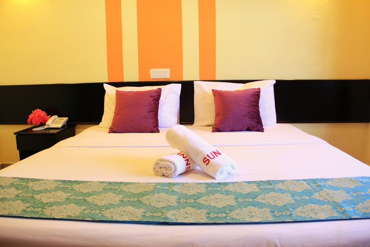 Quarto de hotel com cama bem arrumada, telefone na mesinha de cabeceira e parede com listras verticais.