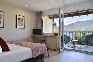 Quarto com cama, escrivaninha, cadeira e varanda com vista para a paisagem.