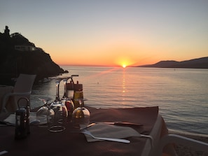 Mesa posta para refeição com vista para o pôr do sol sobre a água.
