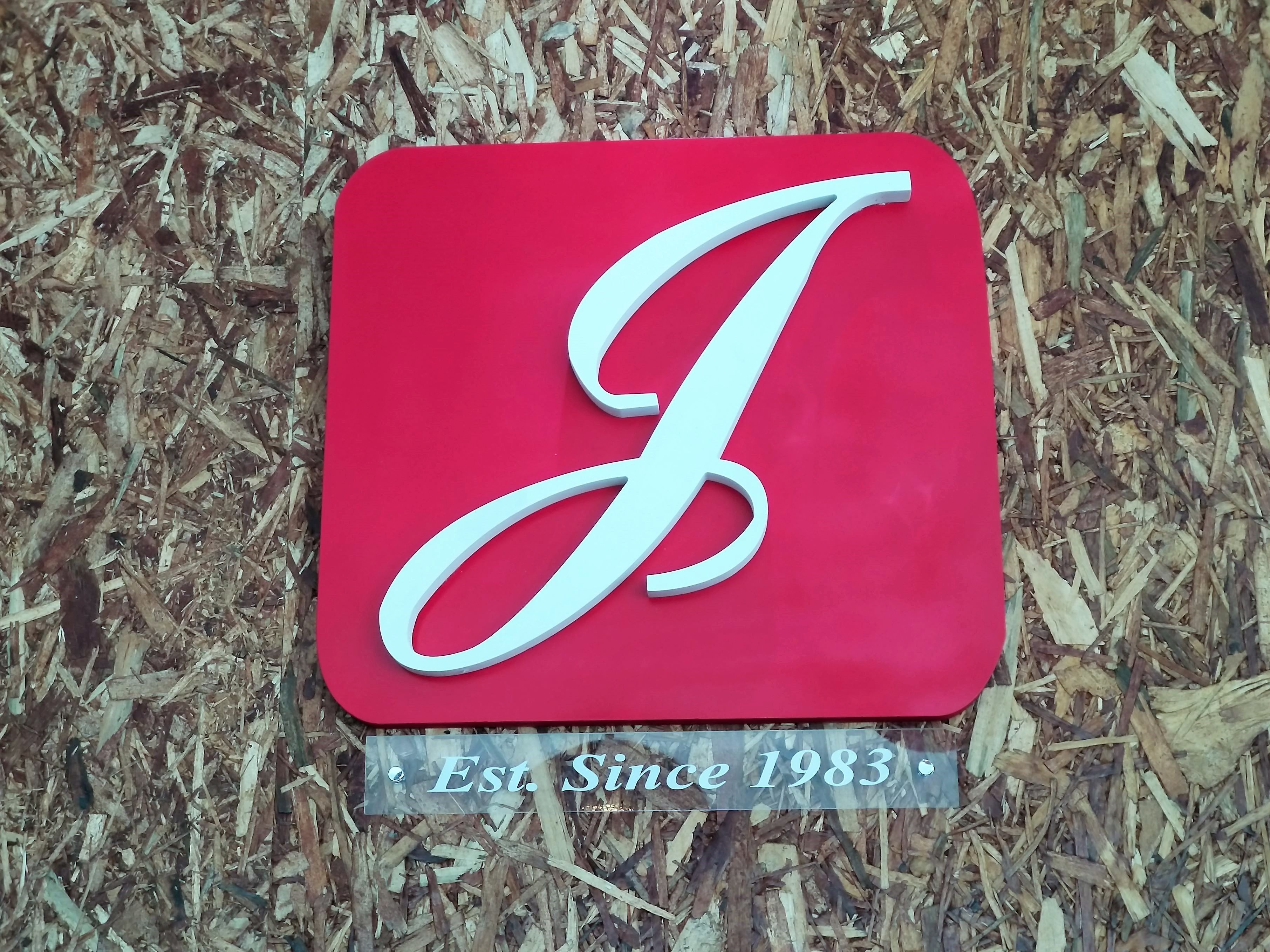 Um letreiro vermelho com uma letra “J” cursiva branca e uma placa indicando 'Est. Desde 1983'.
