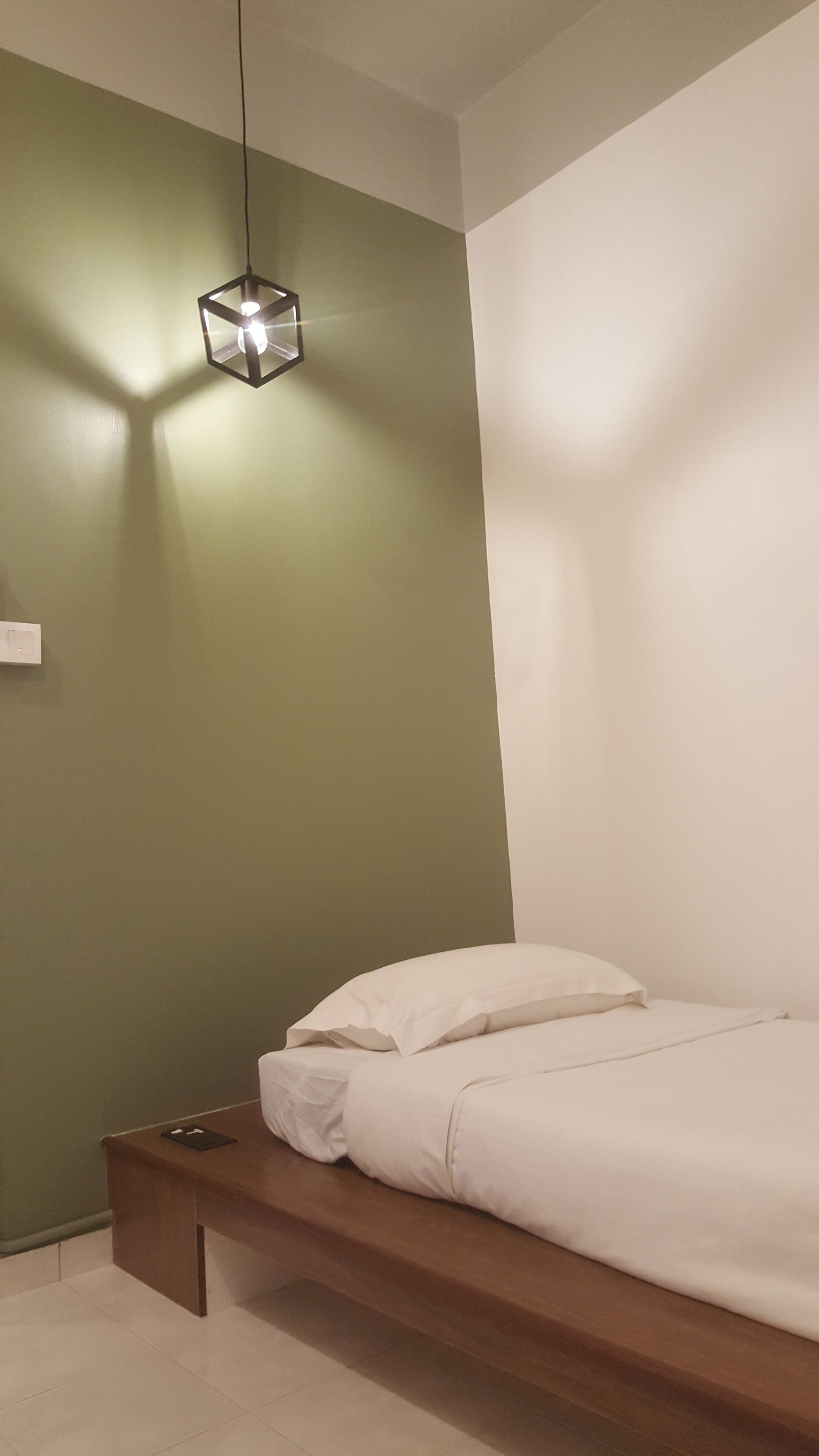 Quarto com cama, mesa de cabeceira, luminária pendente e interruptor de parede.