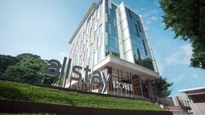 Um edifício moderno de hotel com um letreiro de destaque 'allstay hotel', grandes janelas e telhado plano.