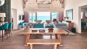 Uma sala de estar ampla com uma mesa de jantar de madeira, cadeiras azuis, um sofá e vista para o oceano.
