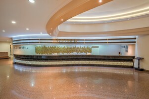Uma área de recepção com balcão de mármore, relógio fixado na parede e placa com a inscrição 'RECEPTION'.