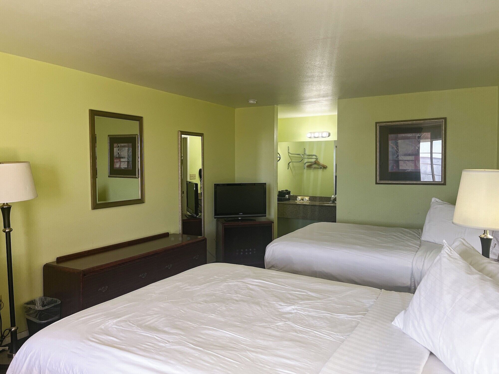 Quarto de hotel com duas camas, televisão, escrivaninha, espelho e abajur.