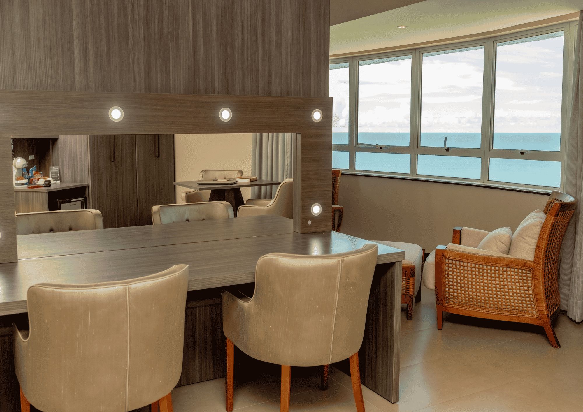 Uma sala de jantar com uma mesa grande, cadeiras e vista para o mar através de amplas janelas.