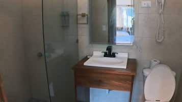 Um banheiro com chuveiro em box de vidro, toucador de madeira com pia, espelho e vaso sanitário.