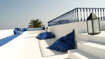 Um terraço exterior branco com almofadas azuis e um candeeiro.