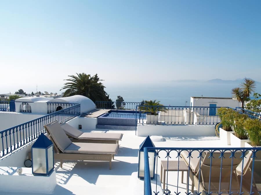 Terraço no topo do edifício com espreguiçadeiras e piscina, com vista para a paisagem urbana costeira.