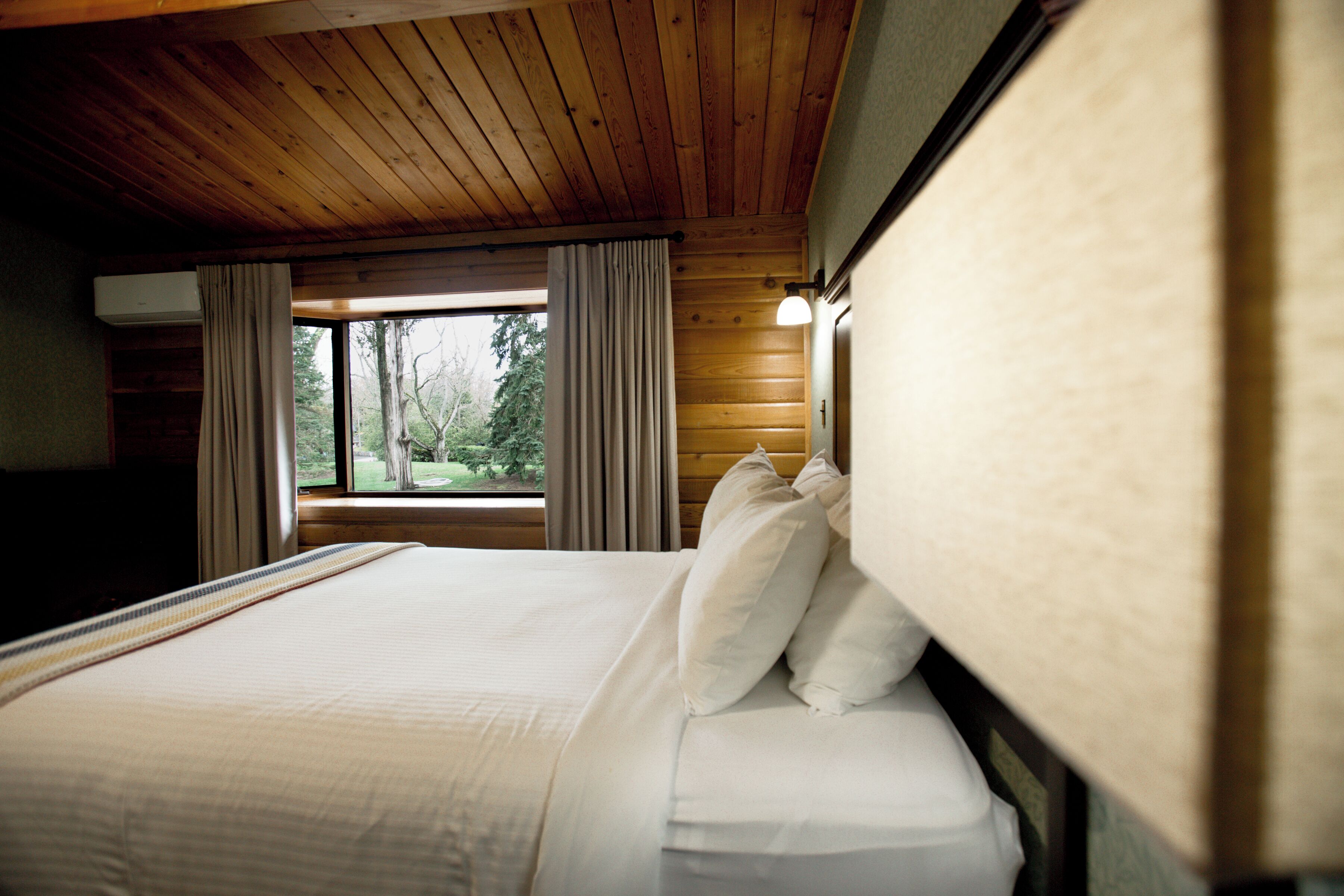 Cama bem arrumada em quarto com paredes de madeira e janela com cortinas.