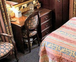 Quarto com cama, cómoda de madeira, cadeira e secretária com espelho.