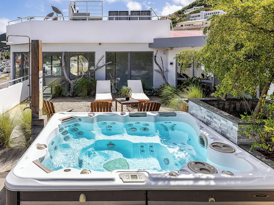 Uma casa moderna com uma banheira de hidromassagem no quintal, rodeada por móveis de exterior e plantas.