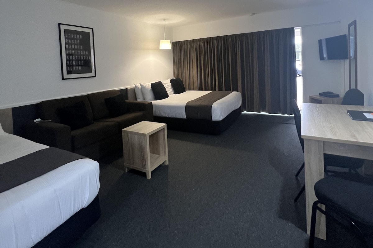 Quarto de hotel com uma cama grande, um sofá, uma mesinha e uma escrivaninha.