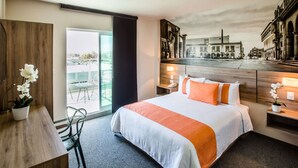 Quarto de hotel com uma cama grande, uma escrivaninha e vista para a paisagem urbana pela janela.