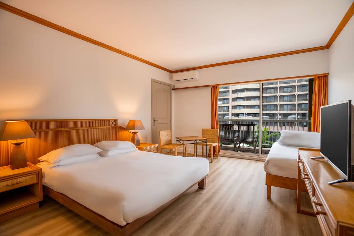 Quarto de hotel com cama grande, escrivaninha, cadeira, televisão e varanda com vista para a cidade.