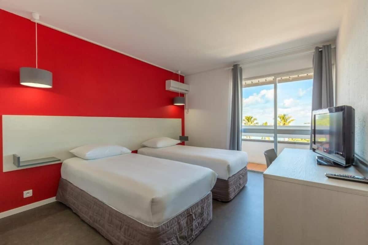 Quarto de hotel com duas camas, televisão e varanda com vista.
