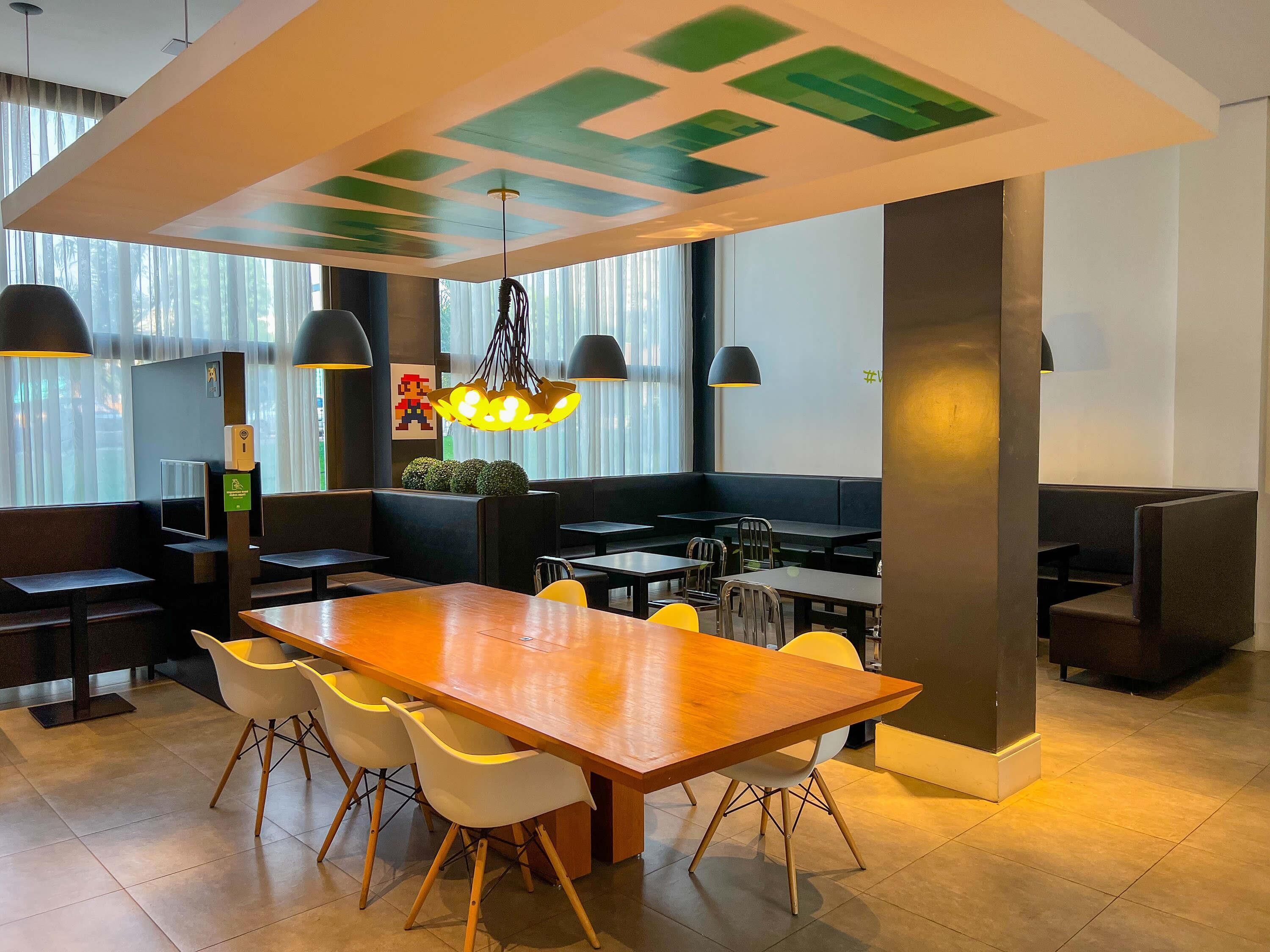 Uma sala de jantar moderna com uma grande mesa de madeira, cadeiras brancas e luminárias pendentes pretas.