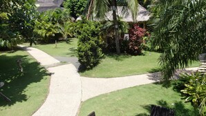 Um jardim tropical com um caminho pavimentado, palmeiras e uma estrutura com telhado de palha.