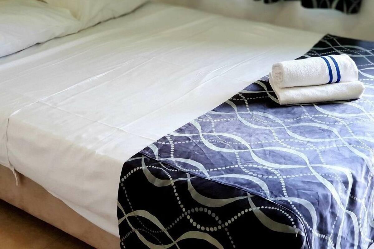 Cama bem arrumada com lençóis brancos e colcha estampada em azul escuro.