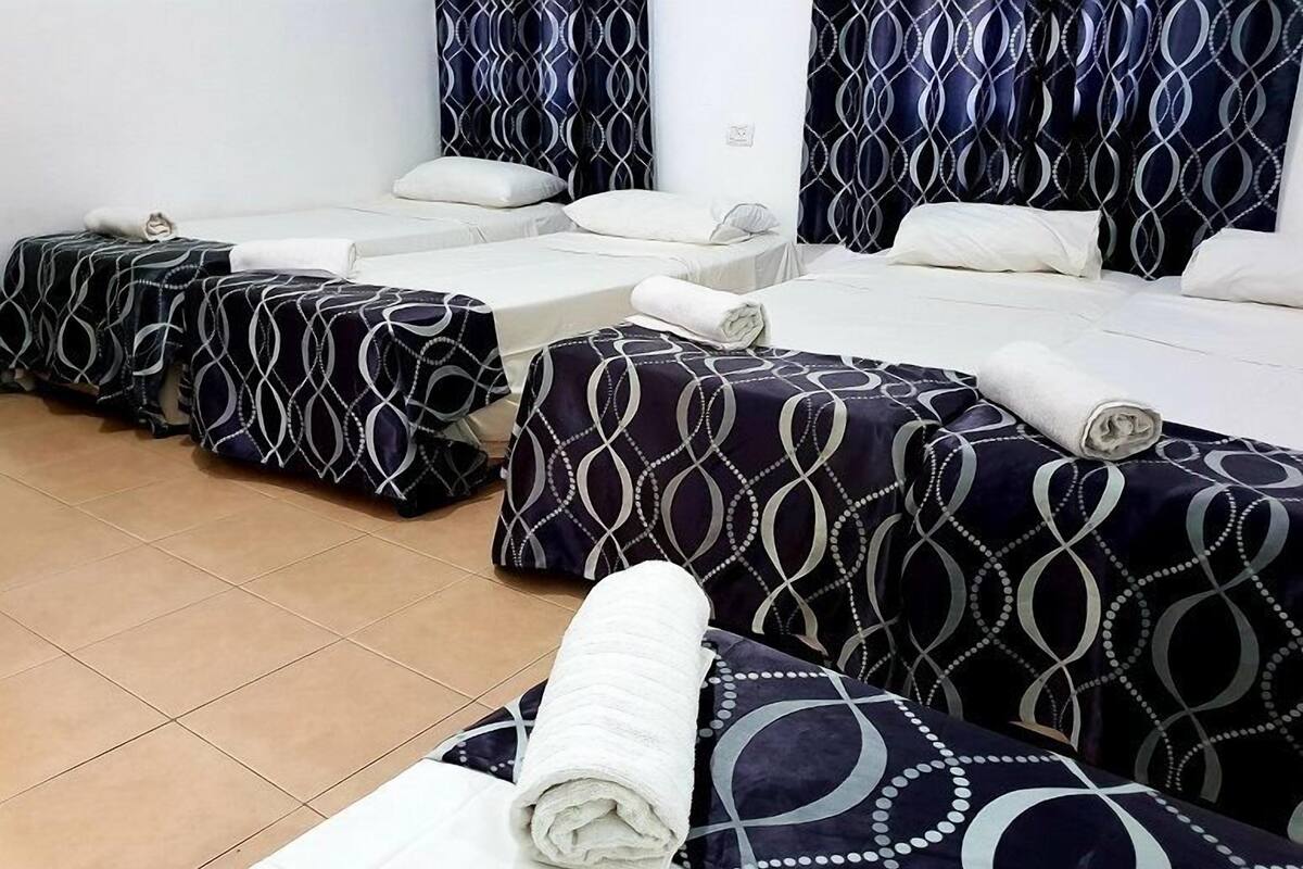 Quarto de hotel com várias camas, cada uma com colcha estampada e almofadas brancas.