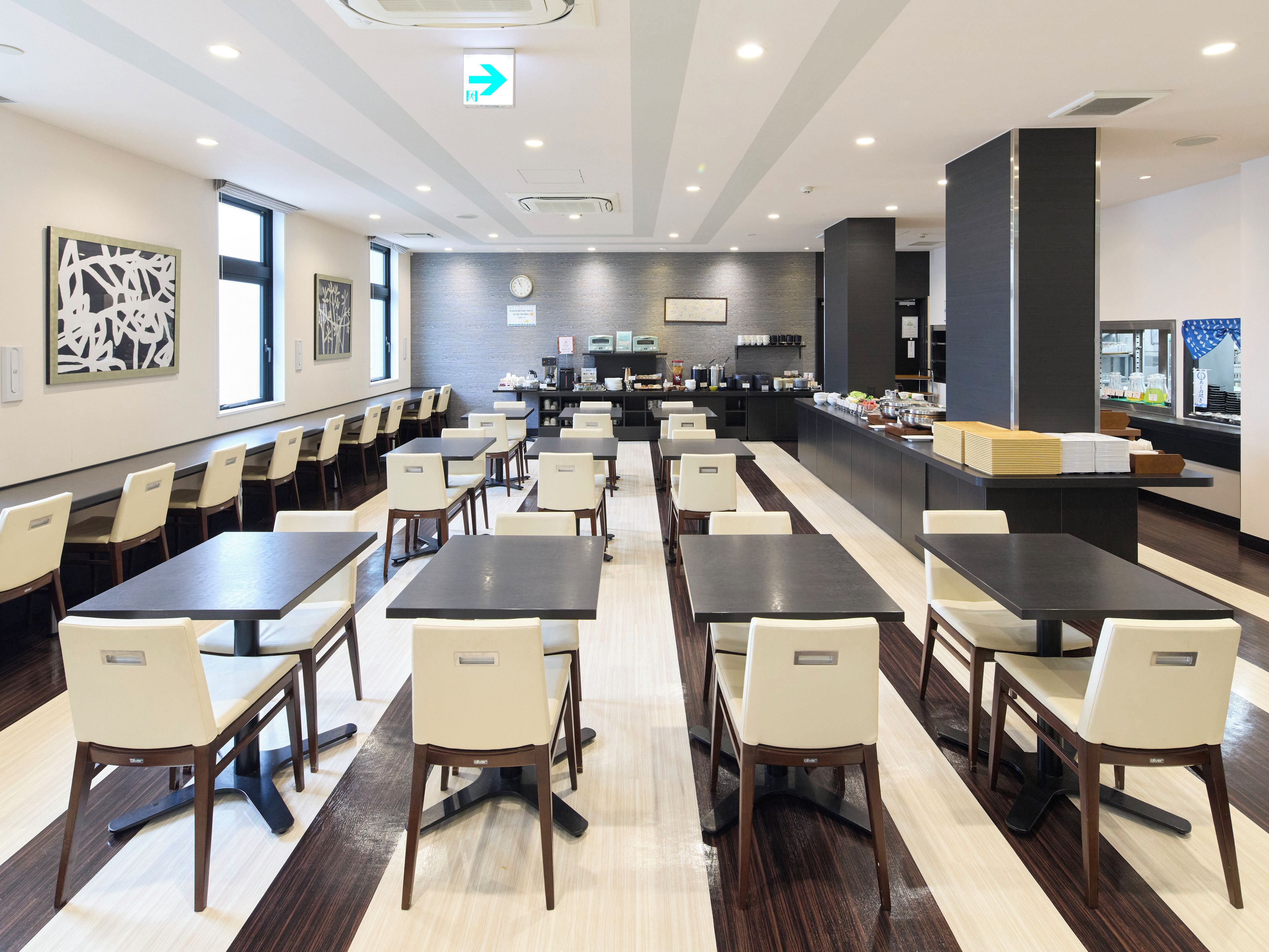 Uma sala de jantar moderna com várias mesas e cadeiras, balcão de cozinha com alimentos e um relógio na parede.