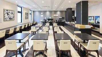 Uma sala de jantar moderna com várias mesas e cadeiras, balcão de cozinha com alimentos e um relógio na parede.