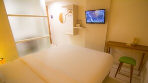 Quarto de hotel com uma cama, uma televisão na parede, uma secretária pequena com uma cadeira e um espelho sobre a secretária.