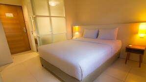 Quarto de hotel com uma cama, abajures, uma porta de madeira e piso de azulejos.