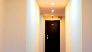 Um corredor estreito com uma porta preta identificada com o número 402 e uma câmera de segurança acima.