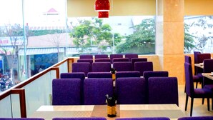 Restaurante com assentos roxos, luminária pendente vermelha e vista para o exterior.