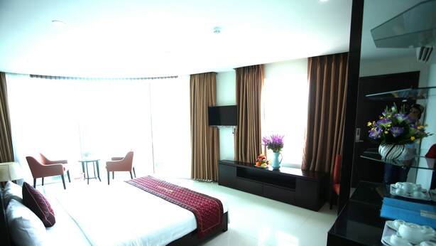 Quarto de hotel com uma cama grande, uma escrivaninha, uma televisão e um espaço de estar com cadeiras.