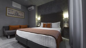 Quarto de hotel moderno com uma cama grande, um sofá e duas luminárias fixadas na parede.