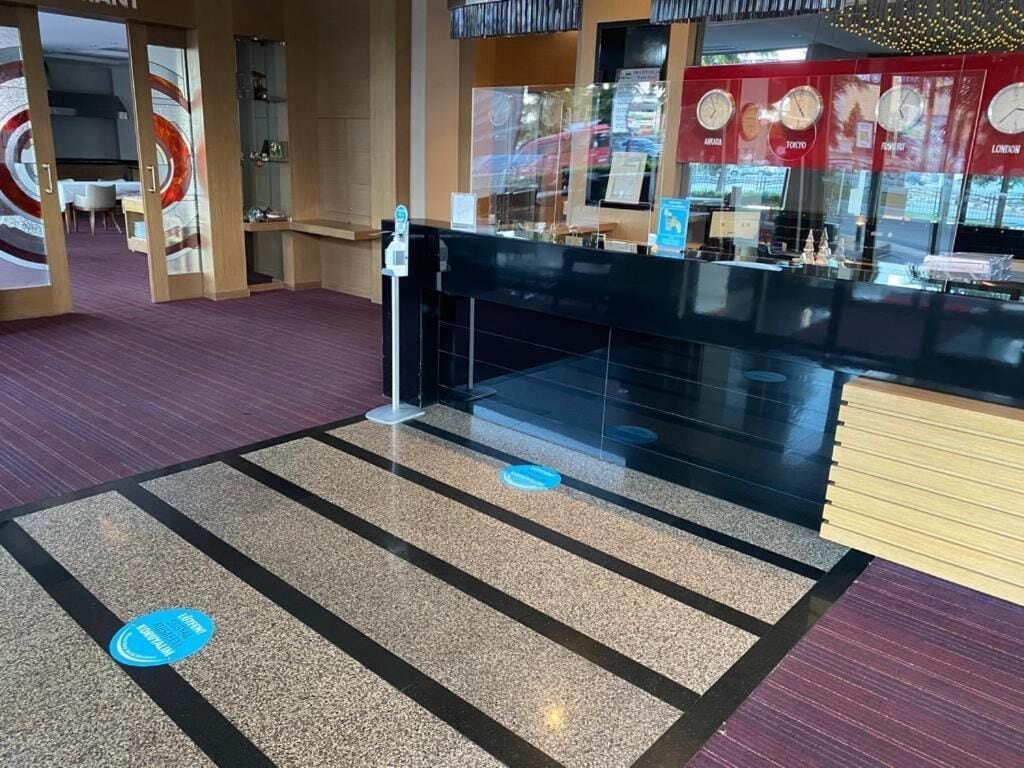 Uma área de recepção com divisória de vidro, um relógio e uma placa indicando a hora em Tóquio.