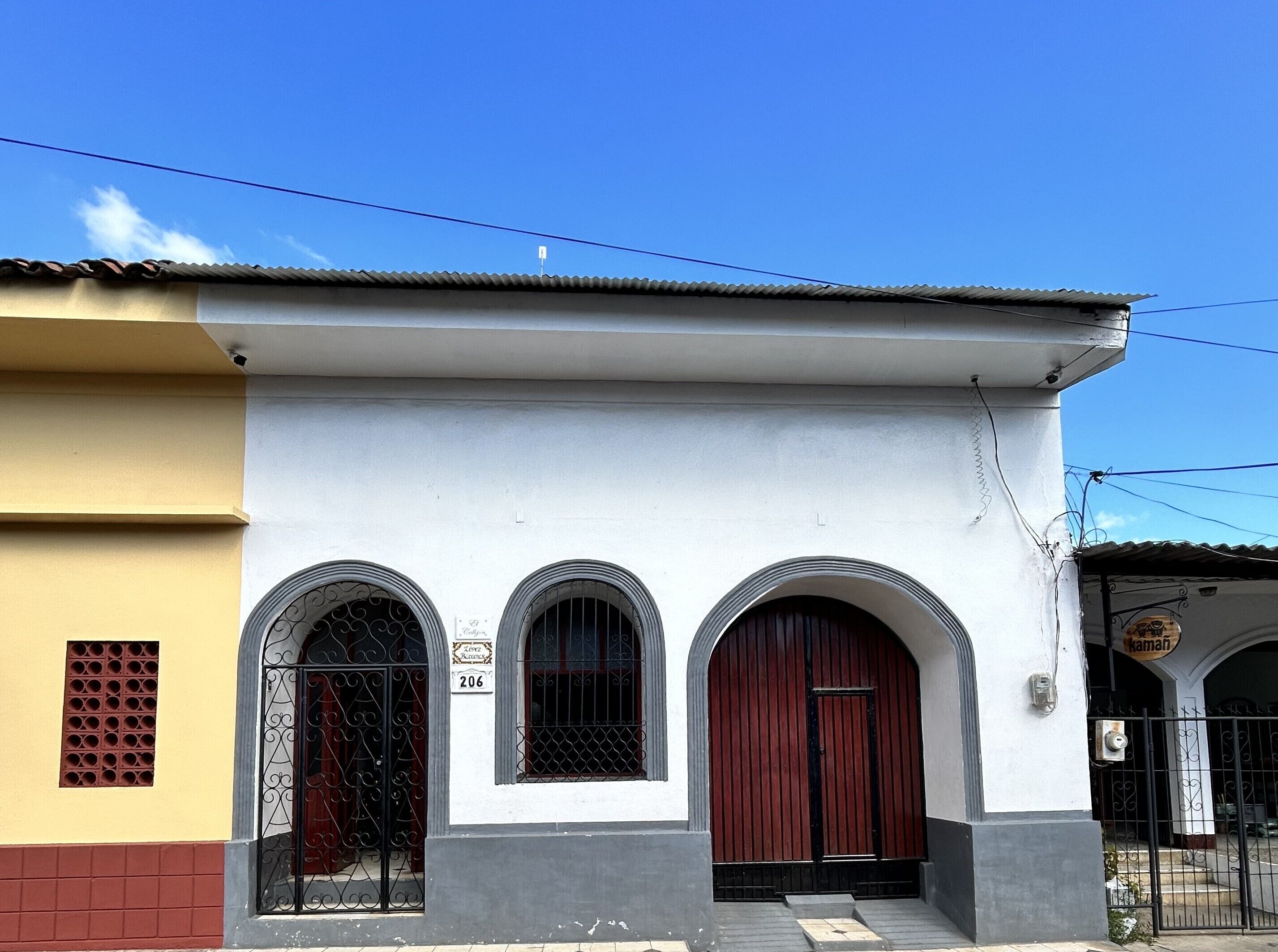 Um edifício com três janelas em arco e uma porta vermelha, uma placa com o número 206, e uma pequena entrada com degraus.