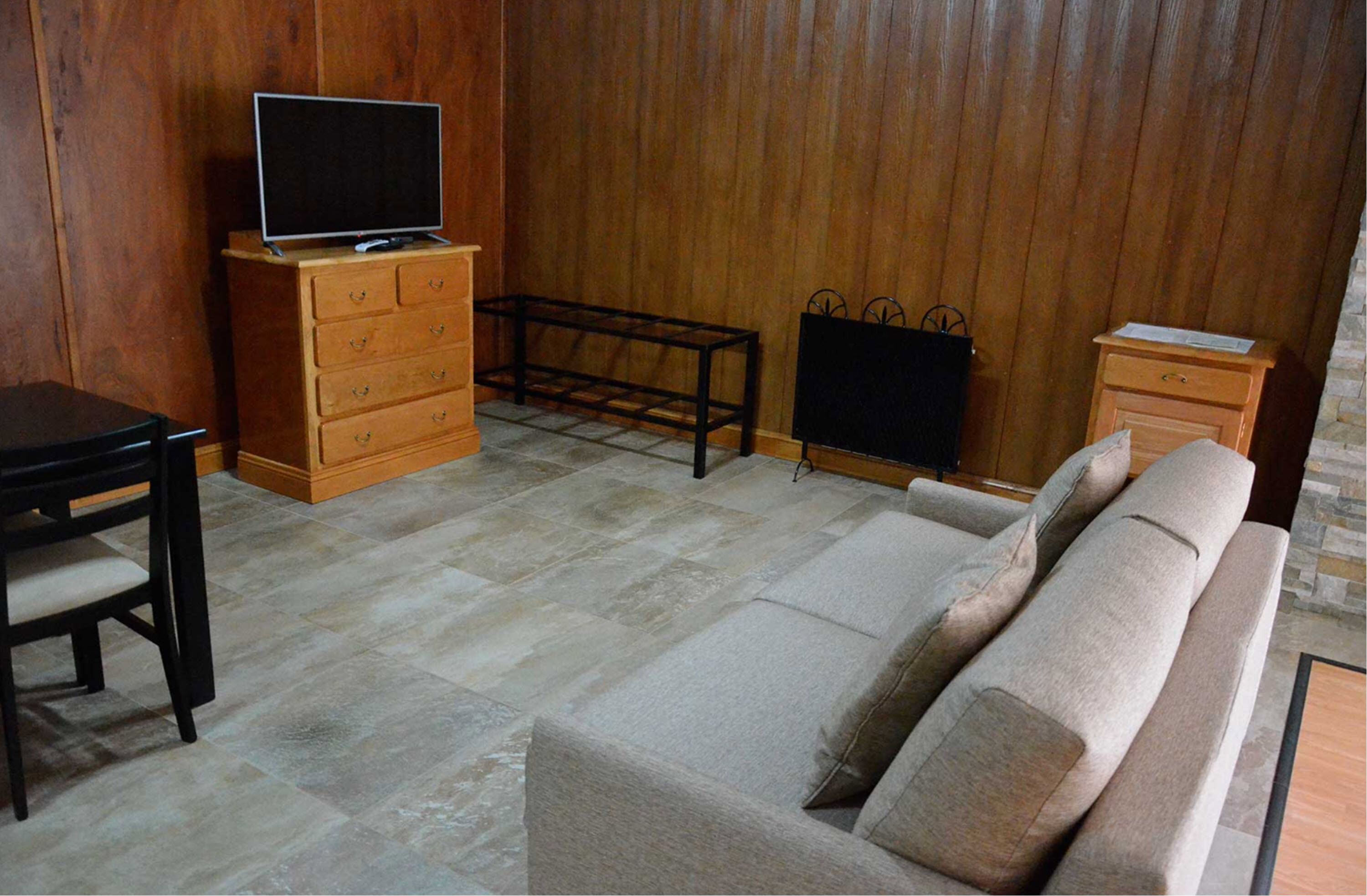 Uma sala de estar com sofá bege, um rack de madeira, uma mesinha e uma lareira.